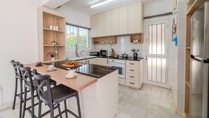 Uma cozinha moderna com uma ilha central, banquetas, estantes embutidas e uma geladeira.