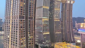 Um edifício alto com um topo curvo característico, vários andares e um terraço no telhado com assentos.