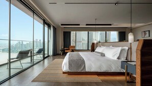 Quarto de hotel moderno com uma cama grande, vista para a cidade e varanda com uma cadeira.