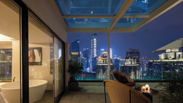 Um banheiro moderno com uma banheira grande e uma varanda envidraçada com vista para a cidade à noite.