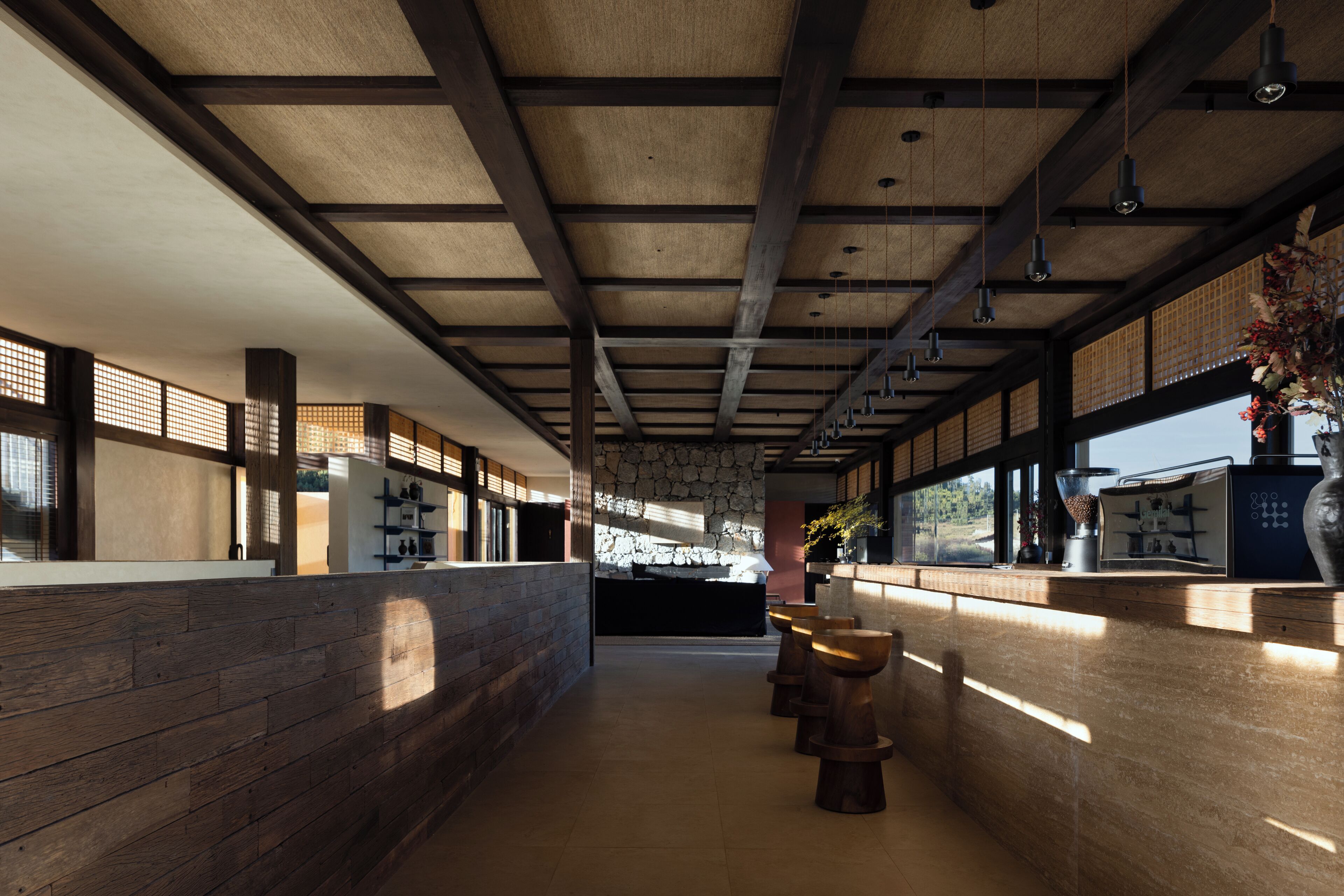 Um interior moderno com vigas de madeira, parede de pedra e um espaço de bar com banquetas.