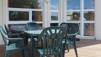 Um pátio externo com mesa e cadeiras, janelas amplas e um deck de madeira.