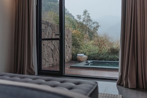 Quarto com uma grande janela, parede de pedra e vista para um jardim com um elemento de água.