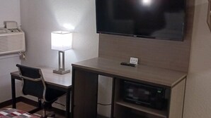 Quarto de hotel com televisão de tela plana na parede, uma mesa com cadeira, luminária e micro-ondas.