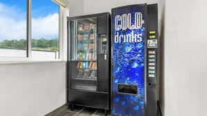 Máquina de vendas com letreiro 'BEBIDAS GELADAS' e vista para a janela.