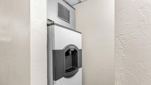 Um dispensador de gelo compacto e moderno num corredor com parede texturizada e chão de madeira.