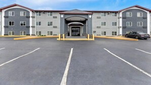 Um hotel moderno de vários andares com entrada central, estacionamento e um único carro estacionado ao lado.