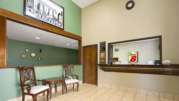 Uma área de recepção com parede verde, duas cadeiras de madeira, um balcão de recepção e um relógio na parede.