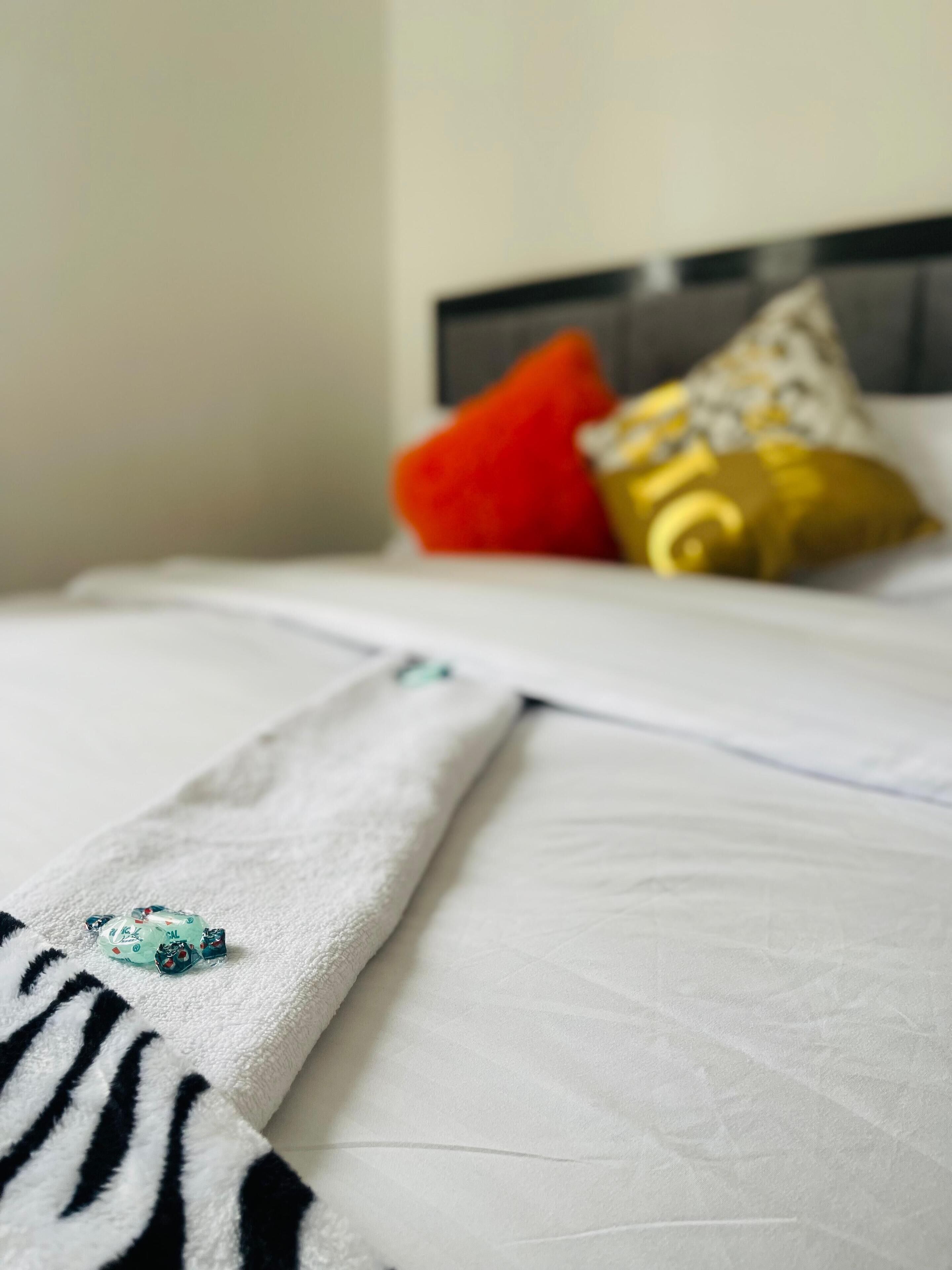 Cama com lençóis brancos, manta estampada em zebra e almofadas decorativas em vermelho e dourado.