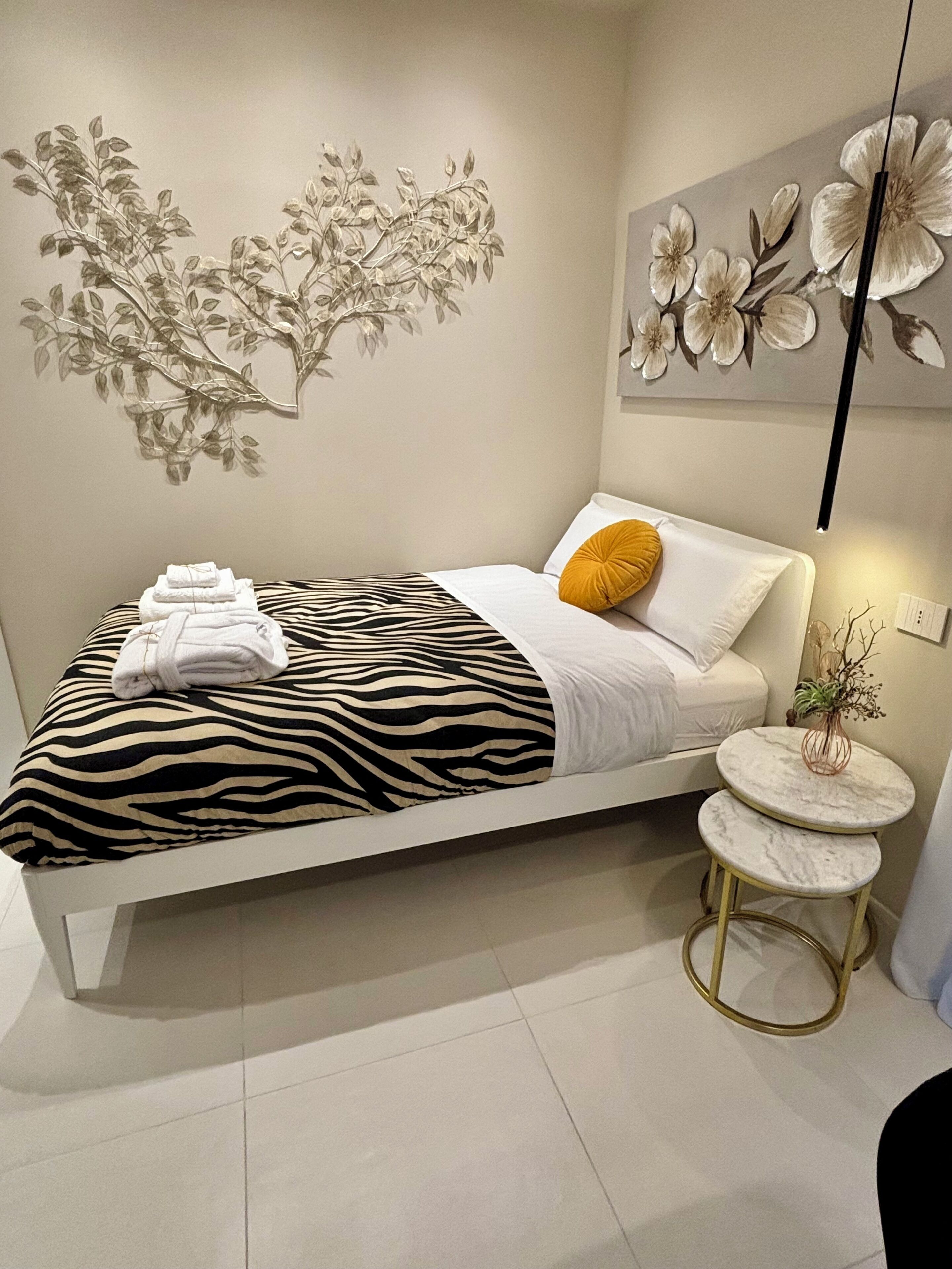 Quarto moderno com colcha estampada em padrão de zebra, travesseiro branco e uma pequena mesa redonda com um vaso.