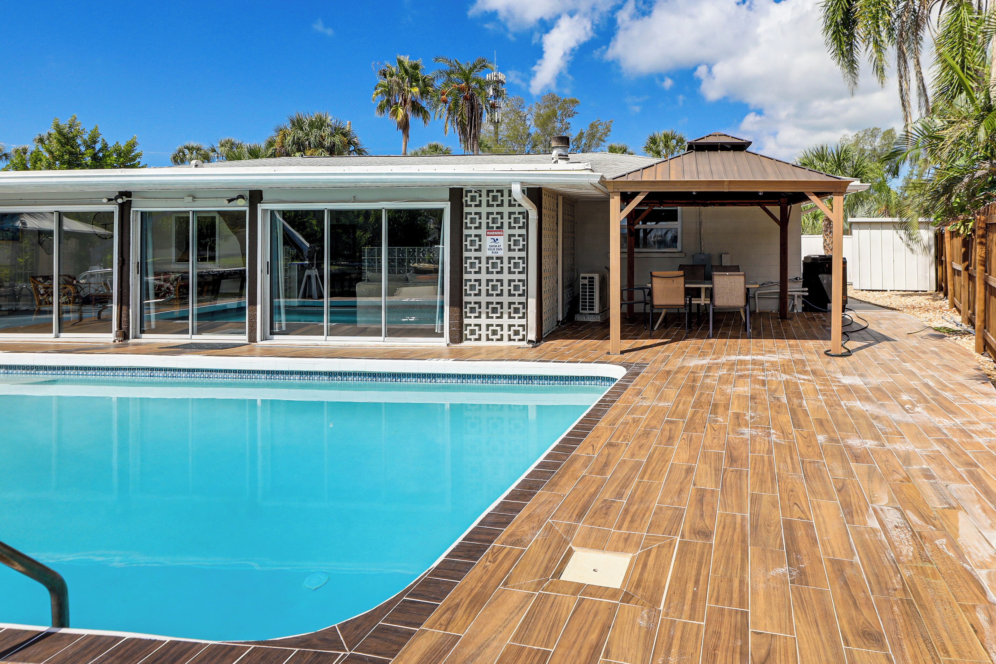 Piscina com deck de madeira, varanda coberta e vista para palmeiras.