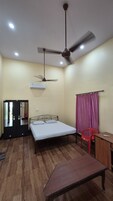 Um quarto com uma cama, um ventilador de teto, uma escrivaninha, uma cadeira e um espelho.