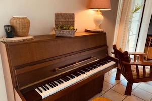 Um piano em um quarto com uma cadeira, uma lâmpada e objetos decorativos sobre uma mesa.