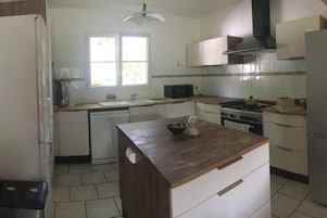 Uma cozinha compacta com armários brancos, bancada de madeira, micro-ondas, fogão e janela que traz luz natural.