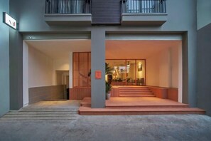 Entrada de um edifício com escadaria que leva a uma varanda no segundo andar.