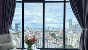 Um quarto com uma janela grande, um sofá, uma mesinha com um vaso de flores e vista para a paisagem urbana.