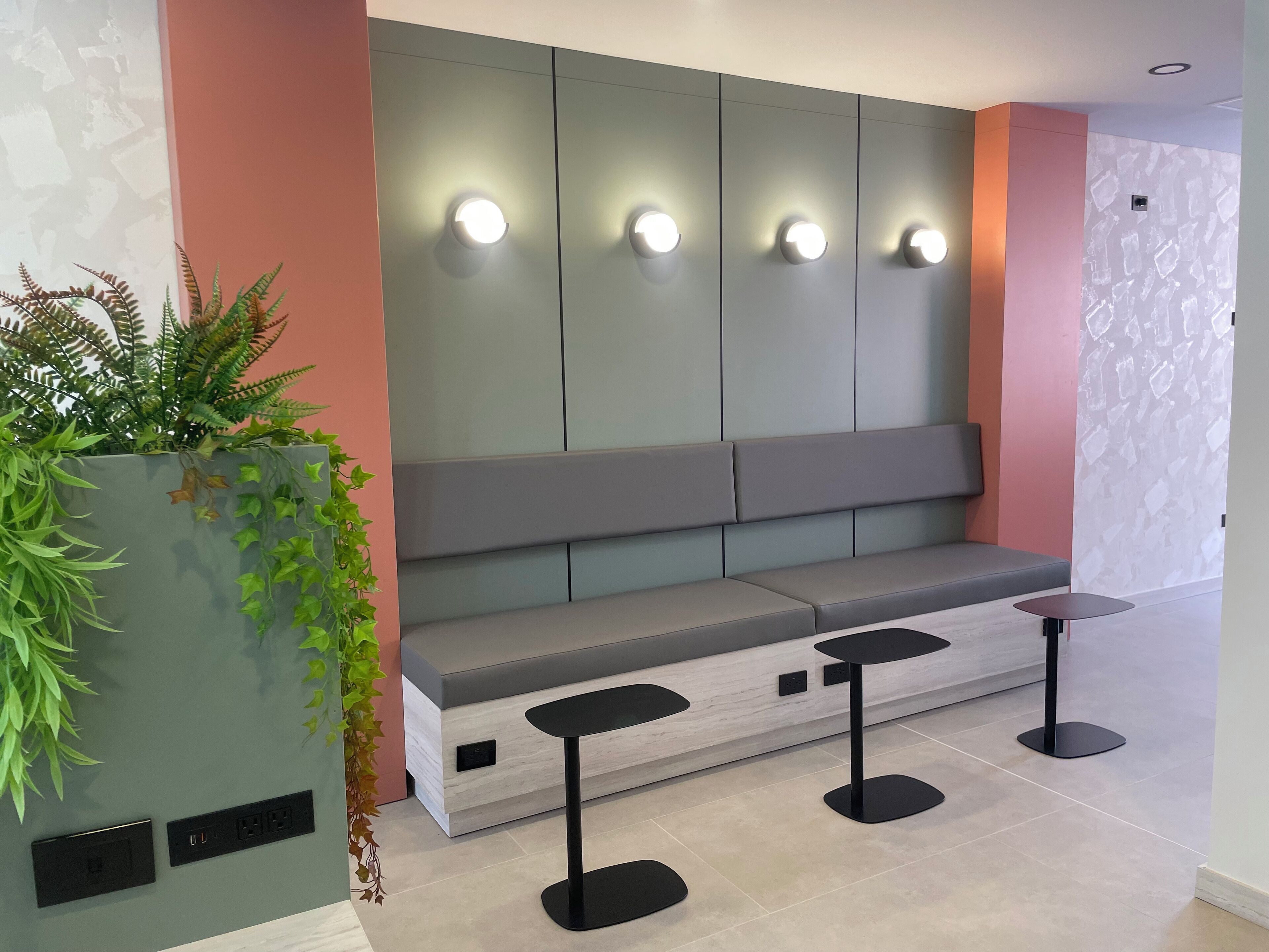 Uma área de espera moderna com um banco cinzento, banquetes pretos e luminárias fixadas na parede.