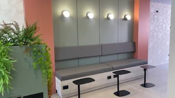 Uma área de espera moderna com um banco cinzento, banquetes pretos e luminárias fixadas na parede.