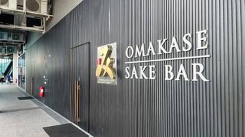 Fachada de um edifício moderno com uma placa indicando 'OMAKASE SAKE BAR' em uma parede texturizada.