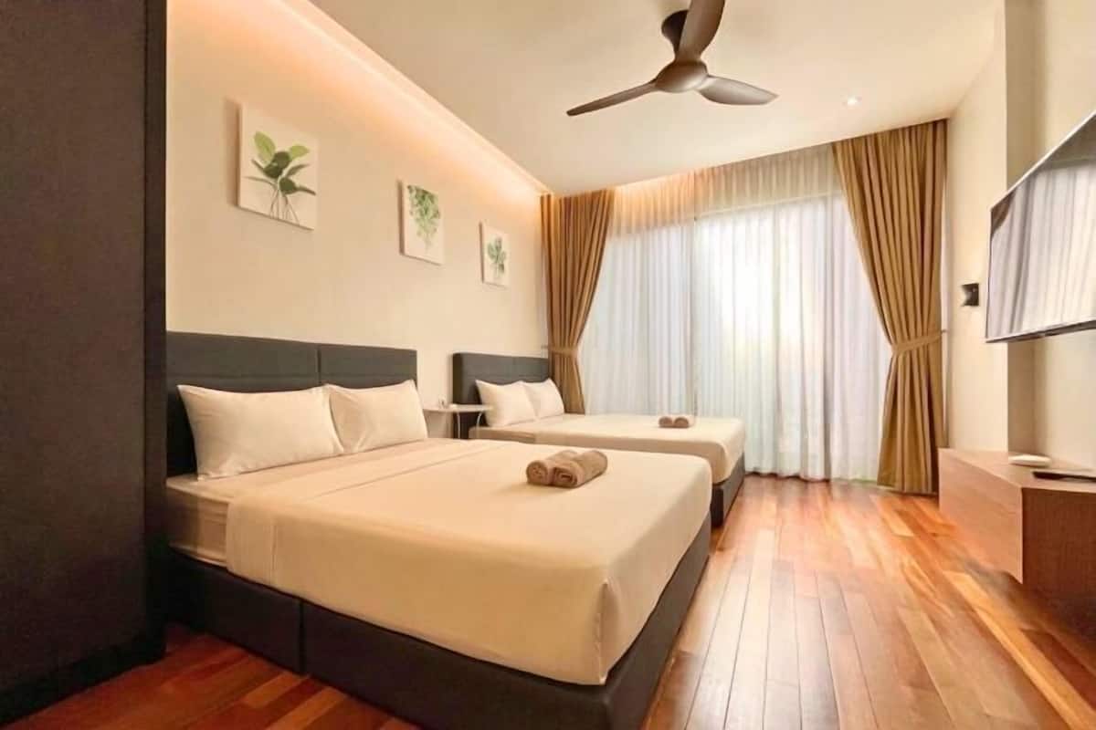 Quarto de hotel com duas camas, ventilador de teto, televisão e uma grande janela com cortinas.