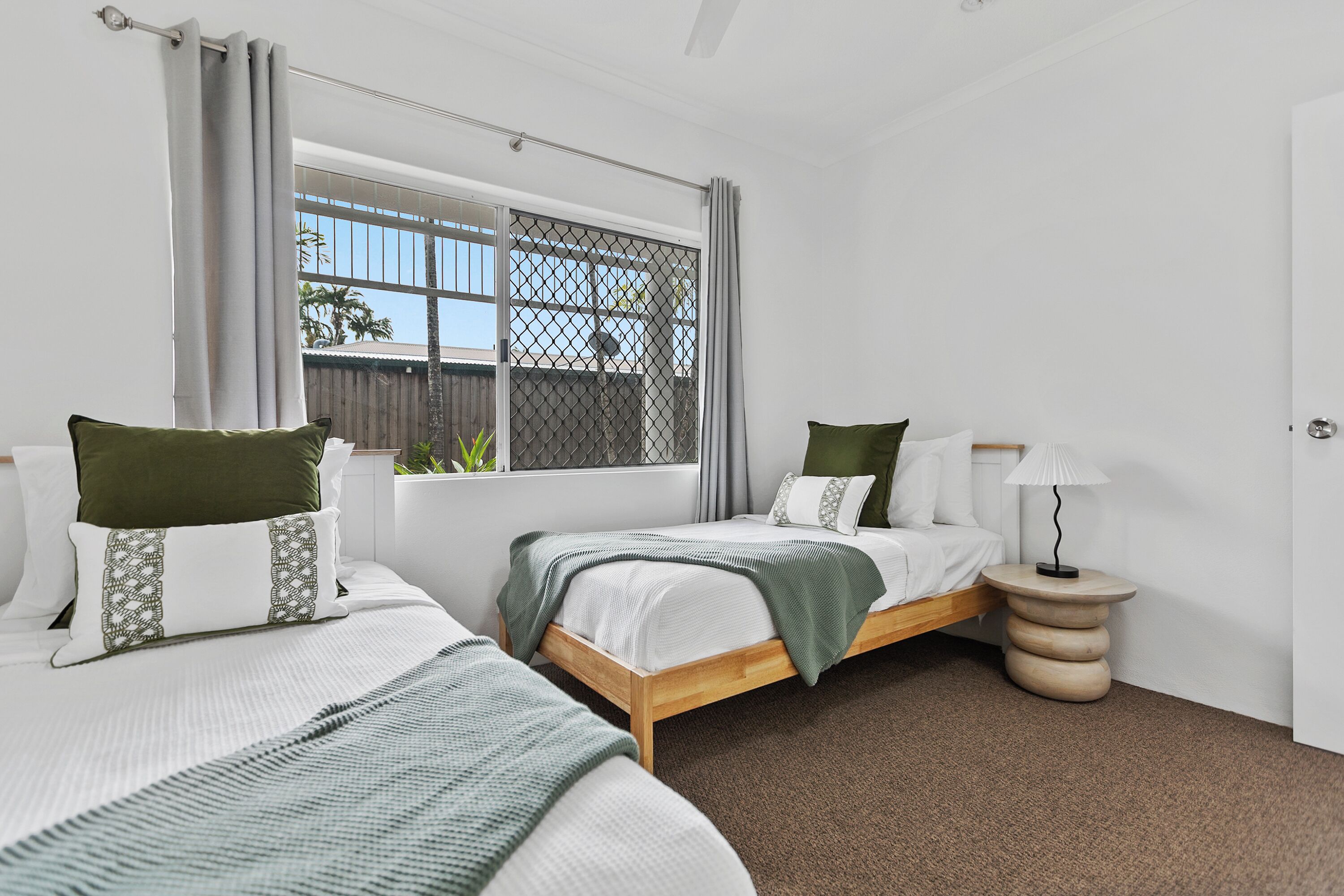 Quarto com duas camas, janela com vista e luminária de cabeceira.
