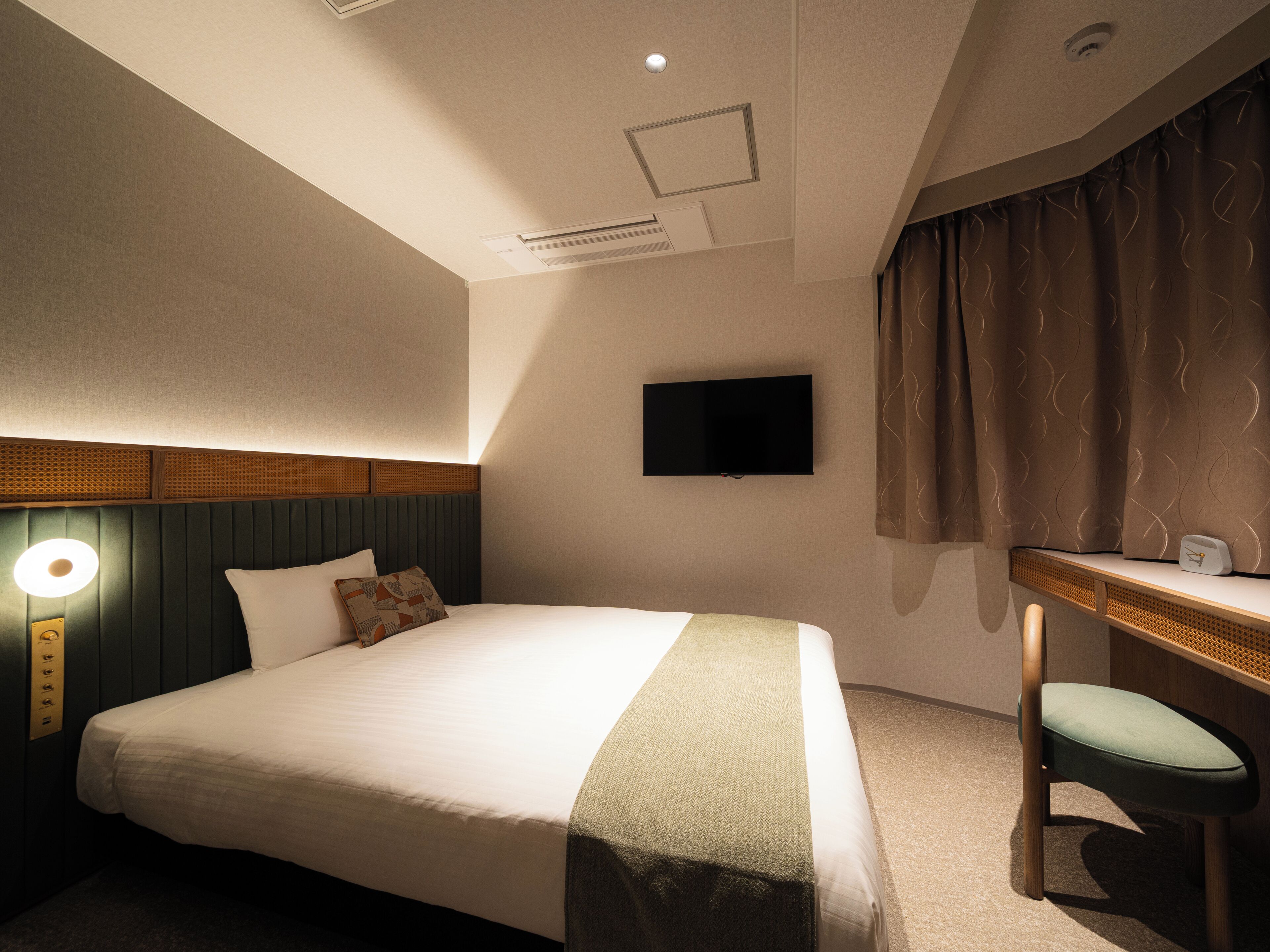 Quarto de hotel com uma cama, escrivaninha, cadeira, televisão e ar condicionado fixado na parede.