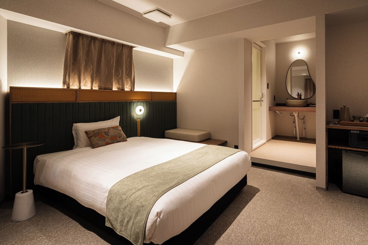 Quarto de hotel com uma cama grande, mesa de cabeceira e escrivaninha com um computador.