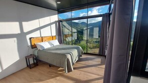 Quarto com uma cama grande, mesa de cabeceira e vista para montanhas por uma porta de vidro deslizante.