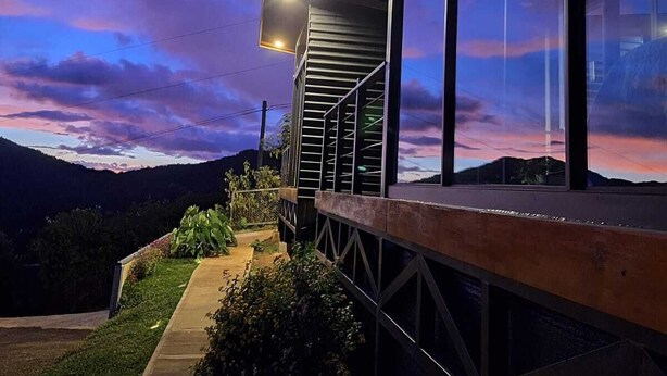 Um edifício moderno com grandes janelas e uma escadaria que leva a um terraço com vista para uma paisagem montanhosa.