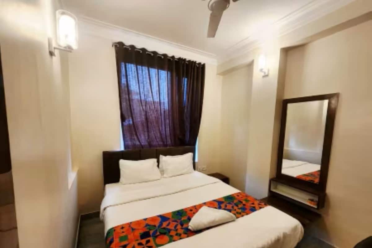 Quarto de hotel com uma cama, um espelho e janela com cortinas.