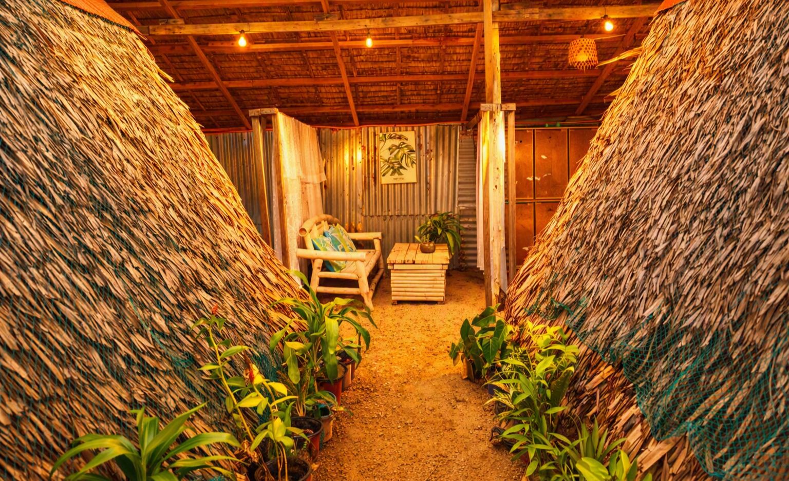 Interior rústico com paredes de palha, um banco de madeira e plantas em vasos.