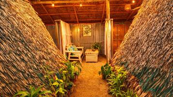 Interior rústico com paredes de palha, um banco de madeira e plantas em vasos.