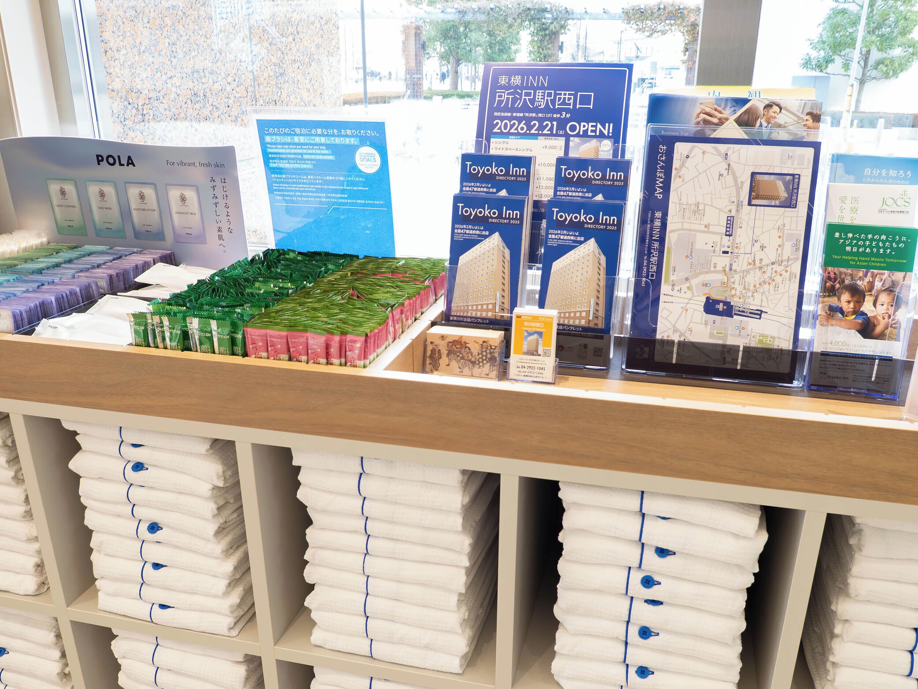 Exposição de hotel com toalhas bem organizadas, uma seção de produtos de skincare POLA e material promocional para Toyoko Inn.