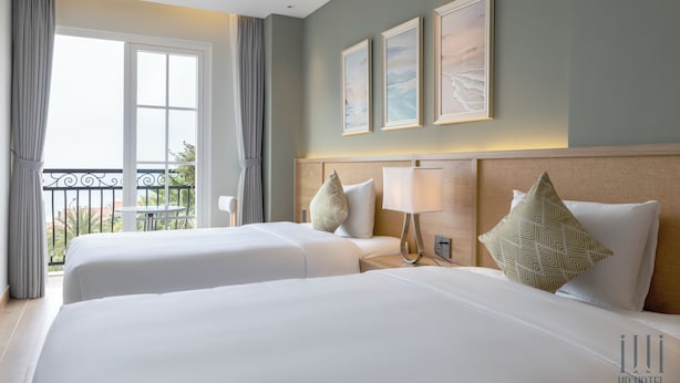 Quarto de hotel com duas camas, varanda e obras de arte na parede.