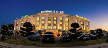 Um hotel chamado 'Sandals Star' com uma placa grande 'GRASLAND', uma placa 'NAMABANK' e vários veículos estacionados em frente.
