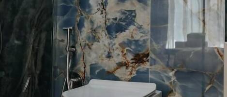 Casa de banho com painel de parede em mármore, sanita, bidé e chuveiro.