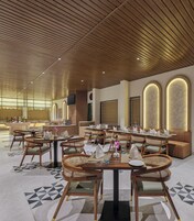 Uma sala de jantar moderna com teto de madeira, mesas redondas e assentos acolchoados.