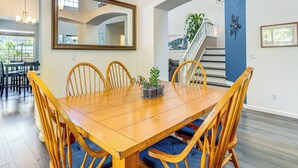 Uma área de refeições com mesa e cadeiras de madeira, um espelho grande e uma escada que leva a um andar superior.
