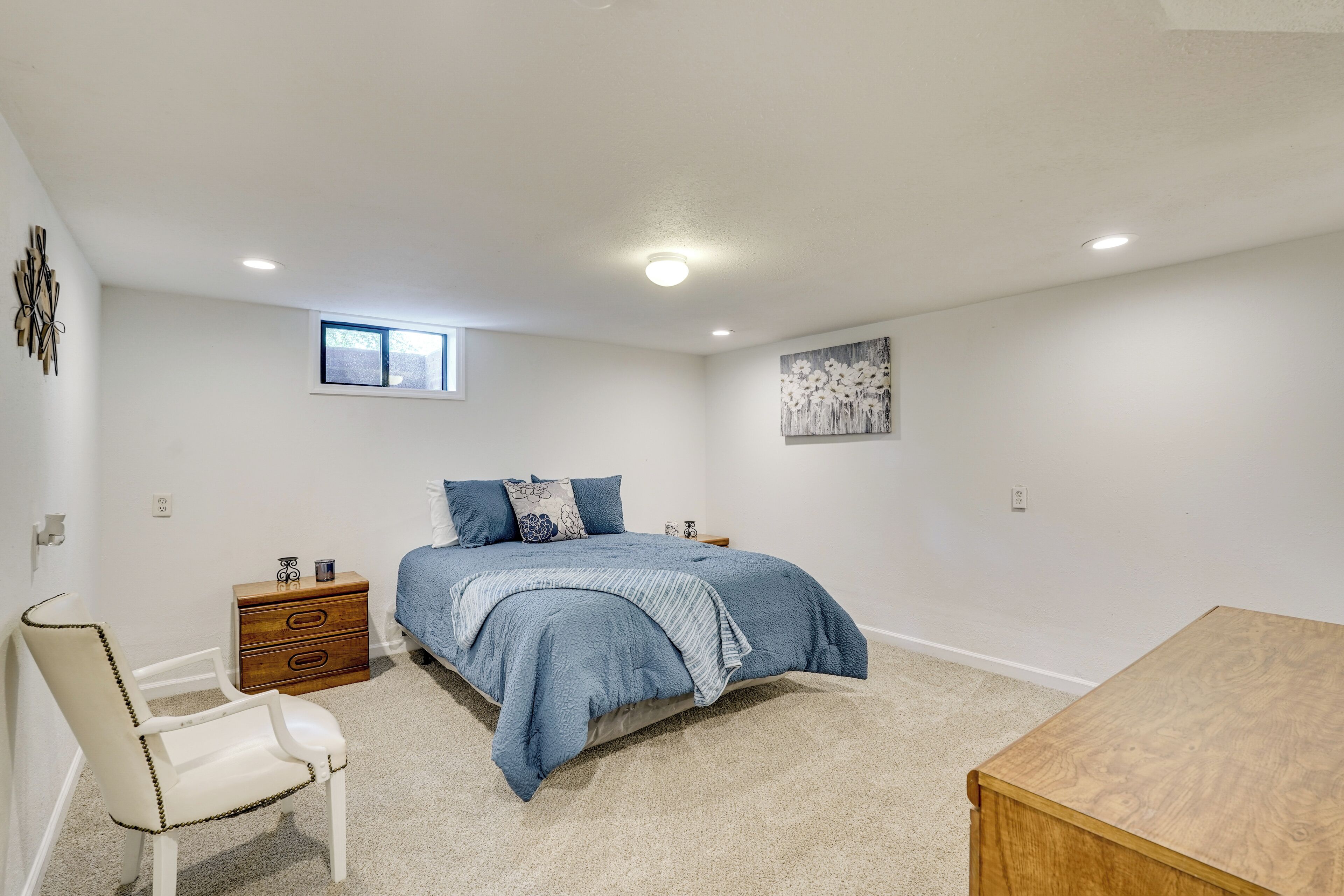 Quarto com cama, escrivaninha, cadeira, cômoda e janela pequena.