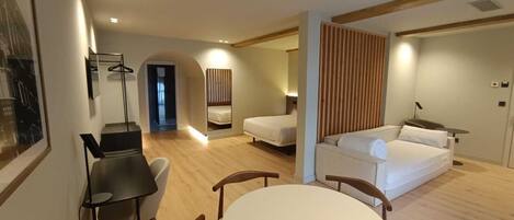 Quarto de hotel moderno com uma mesa de jantar redonda, dois sofás brancos, uma pequena escrivaninha e um espelho.