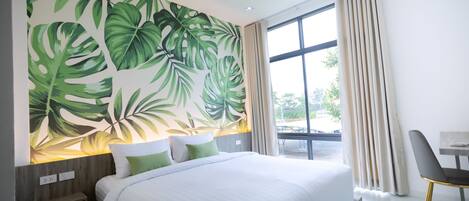 Quarto de hotel com uma cama grande, vista para o exterior através de uma janela e parede com padrão de folhagem tropical.