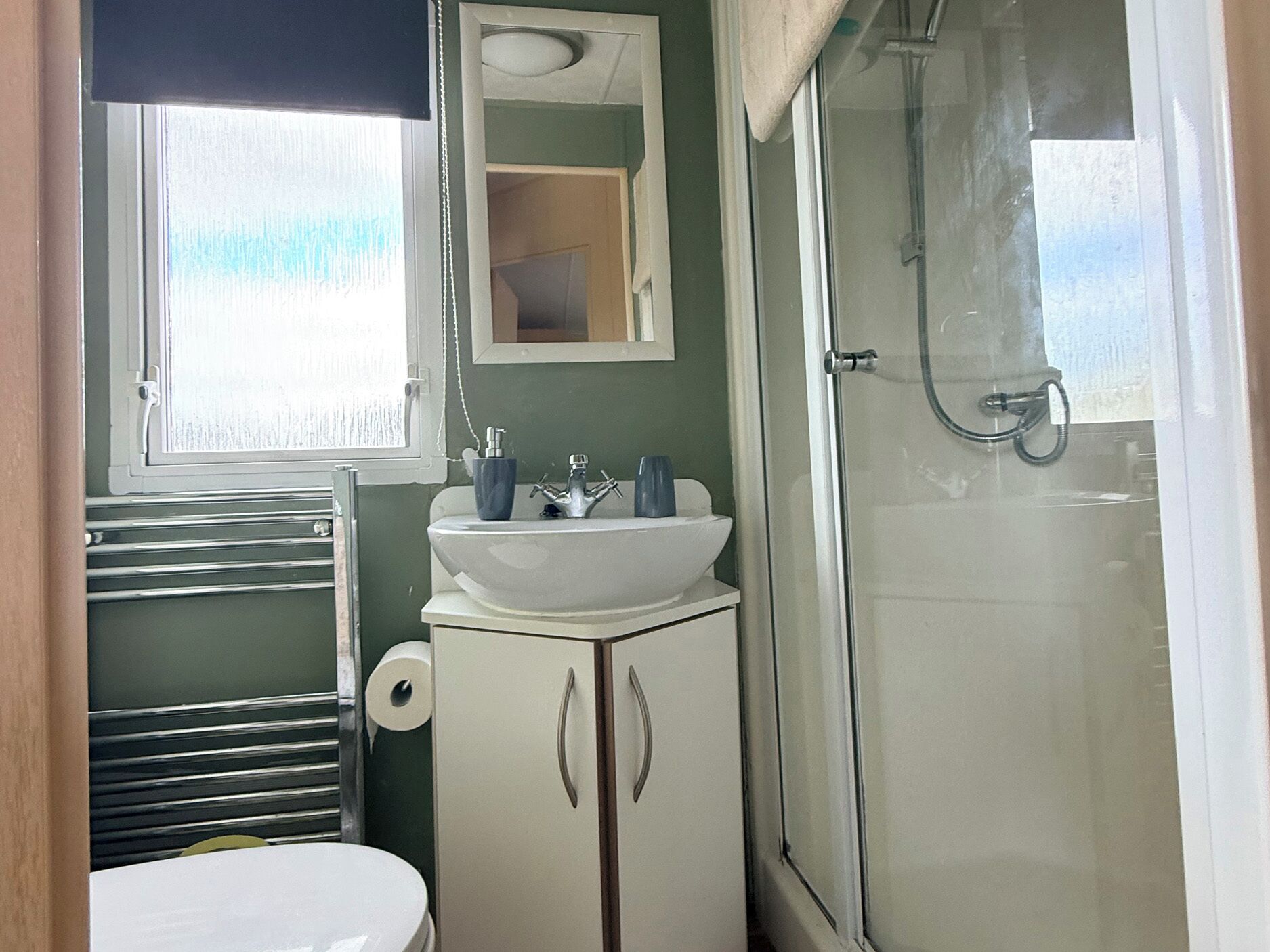 Casa de banho compacta com sanita, lavatório, chuveiro e espelho.
