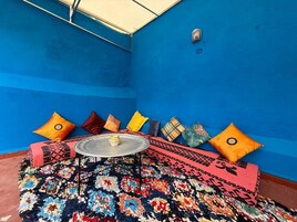 Um quarto com parede azul, tapete estampado, mesa redonda e almofadas coloridas.