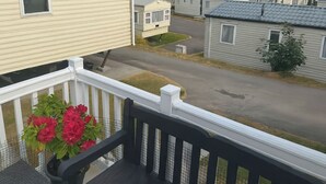 Uma área residencial com várias casas móveis, uma rua pavimentada e uma varanda com guarda-corpo e flores em vasos.