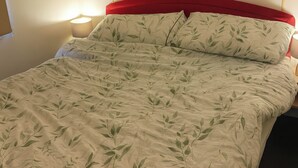Uma cama com colcha estampada em folhas e cabeceira vermelha, acompanhada por duas luminárias de apoio.