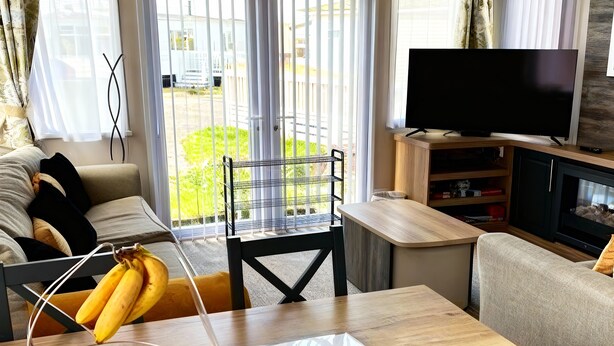 Uma sala de estar moderna com um sofá, uma mesa de centro com um laptop e frutas, uma TV e uma lareira.