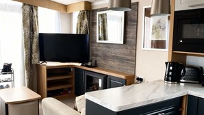 Quarto de hotel moderno com televisão de tela plana, pequena cozinha, área de estar com sofá e lareira.