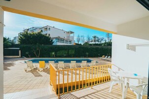Uma área de piscina moderna ao ar livre, com deck de madeira, espreguiçadeiras brancas e guarda-corpo amarelo.