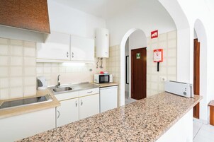 Uma cozinha moderna com armários brancos, bancadas de granito, micro-ondas embutido e aquecedor de água.