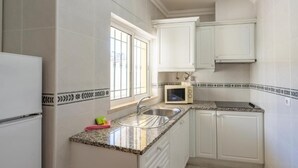 Cozinha compacta com armários brancos, bancada de granito, micro-ondas e janela com persianas.